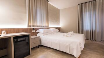 Quarto de hotel com cama, mesa de cabeceira e frigorífico embutido.