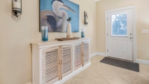 Um corredor com porta branca, uma pintura grande de um pássaro e um console com objetos decorativos.