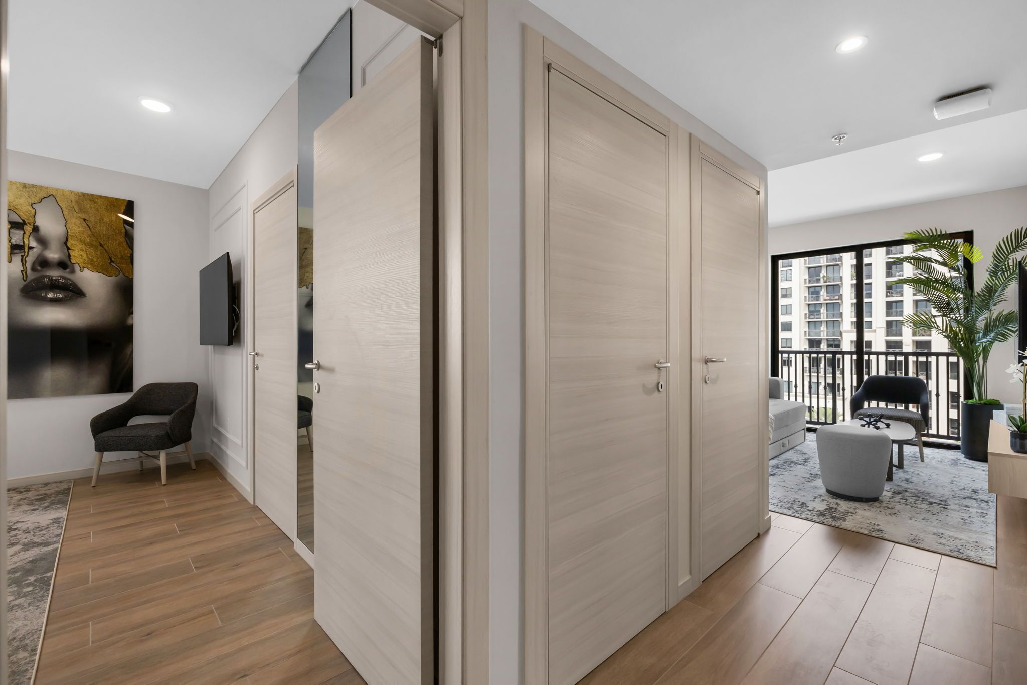 Uma sala de estar moderna com uma grande porta deslizante, uma televisão de tela plana, uma poltrona cinza e vista para uma varanda com uma planta.
