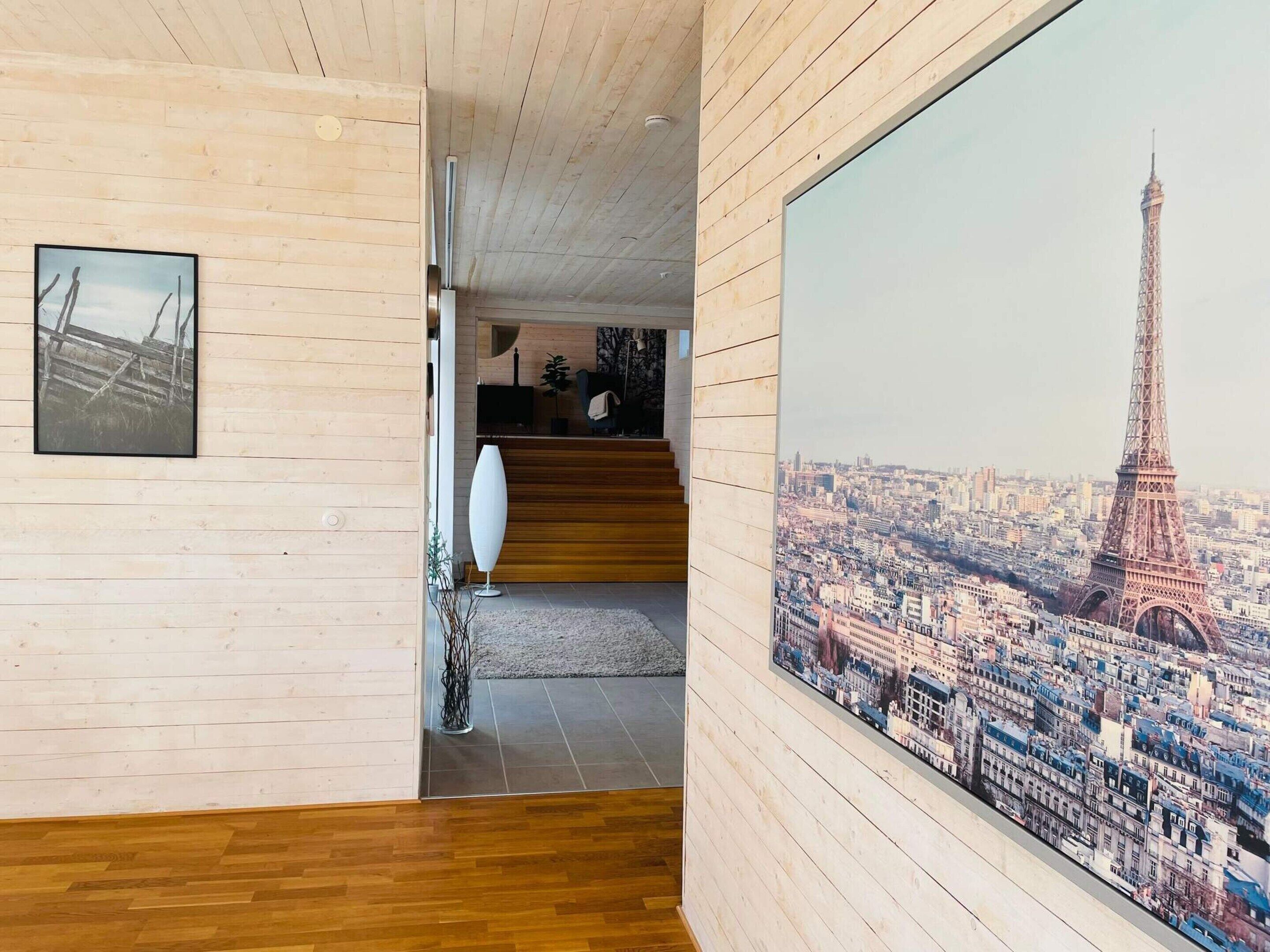 Um interior moderno com paredes de madeira, um grande mural da paisagem urbana e uma escadaria que leva a outro cômodo.
