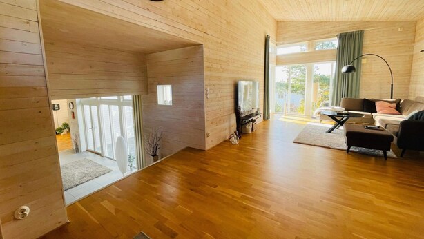 Uma sala de estar ampla com piso de madeira, um relógio grande e um conjunto de sofás moderno.
