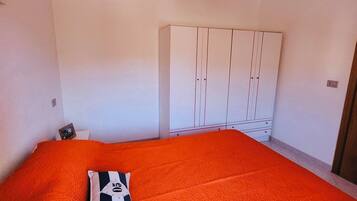 Quarto com cama grande, guarda-roupa branco e luminária suspensa laranja.