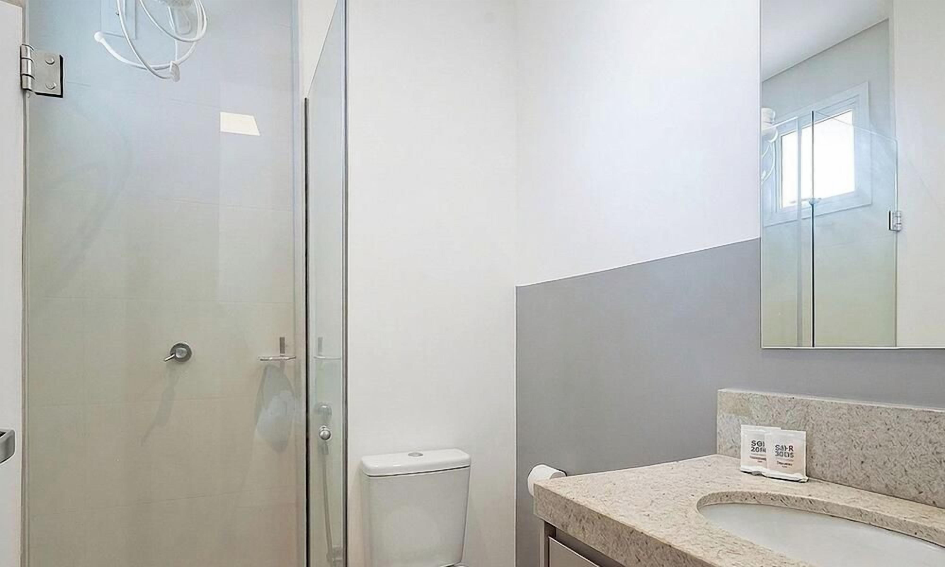 Um banheiro com box de vidro, vaso sanitário e pia com bancada de mármore.