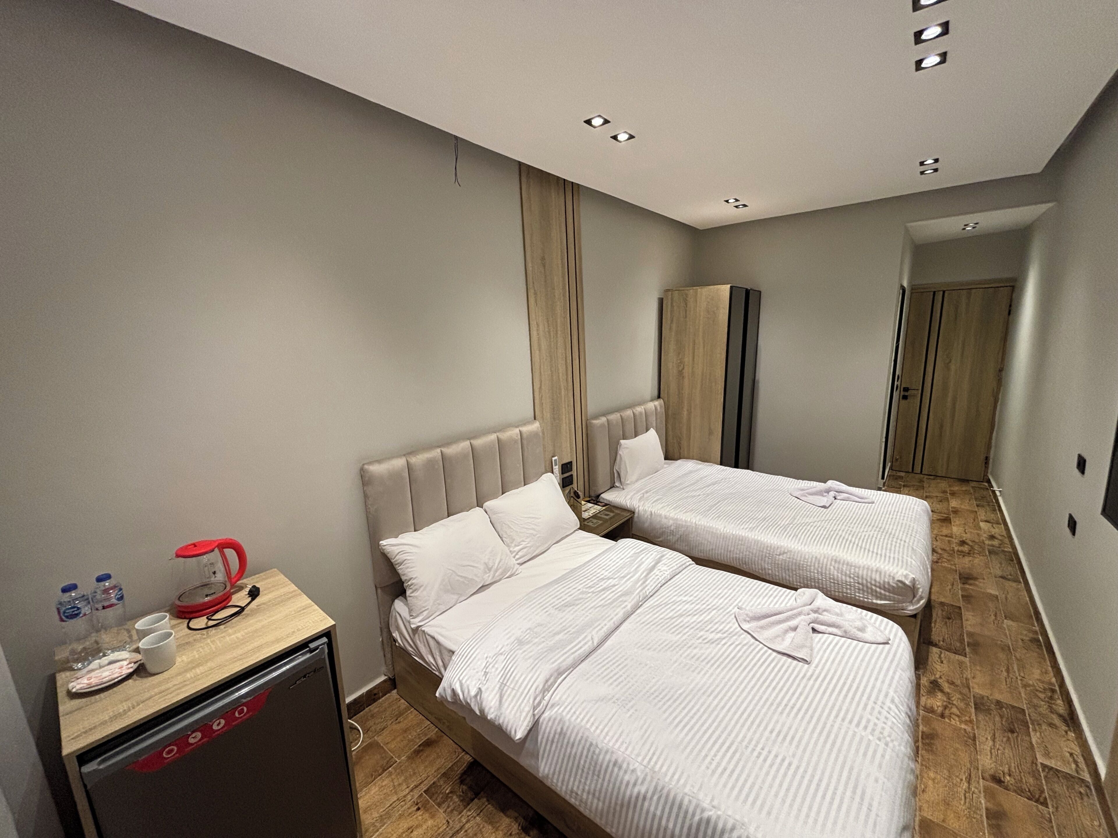 Quarto de hotel com duas camas, uma secretária pequena, um guarda-roupa e a porta do banheiro.