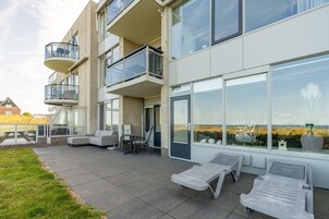 Um edifício de apartamentos moderno com um pátio equipado com mobiliário de exterior e vista para o campo.