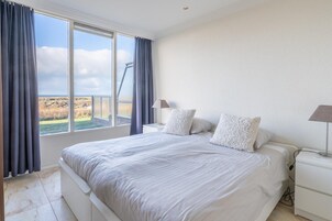 Quarto com cama grande, duas mesas de cabeceira, abajur e vista para o exterior.