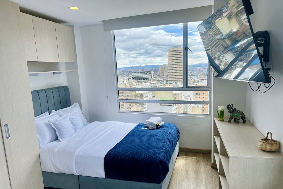 Quarto de hotel moderno com uma cama grande, uma escrivaninha, uma televisão e vista para a cidade.