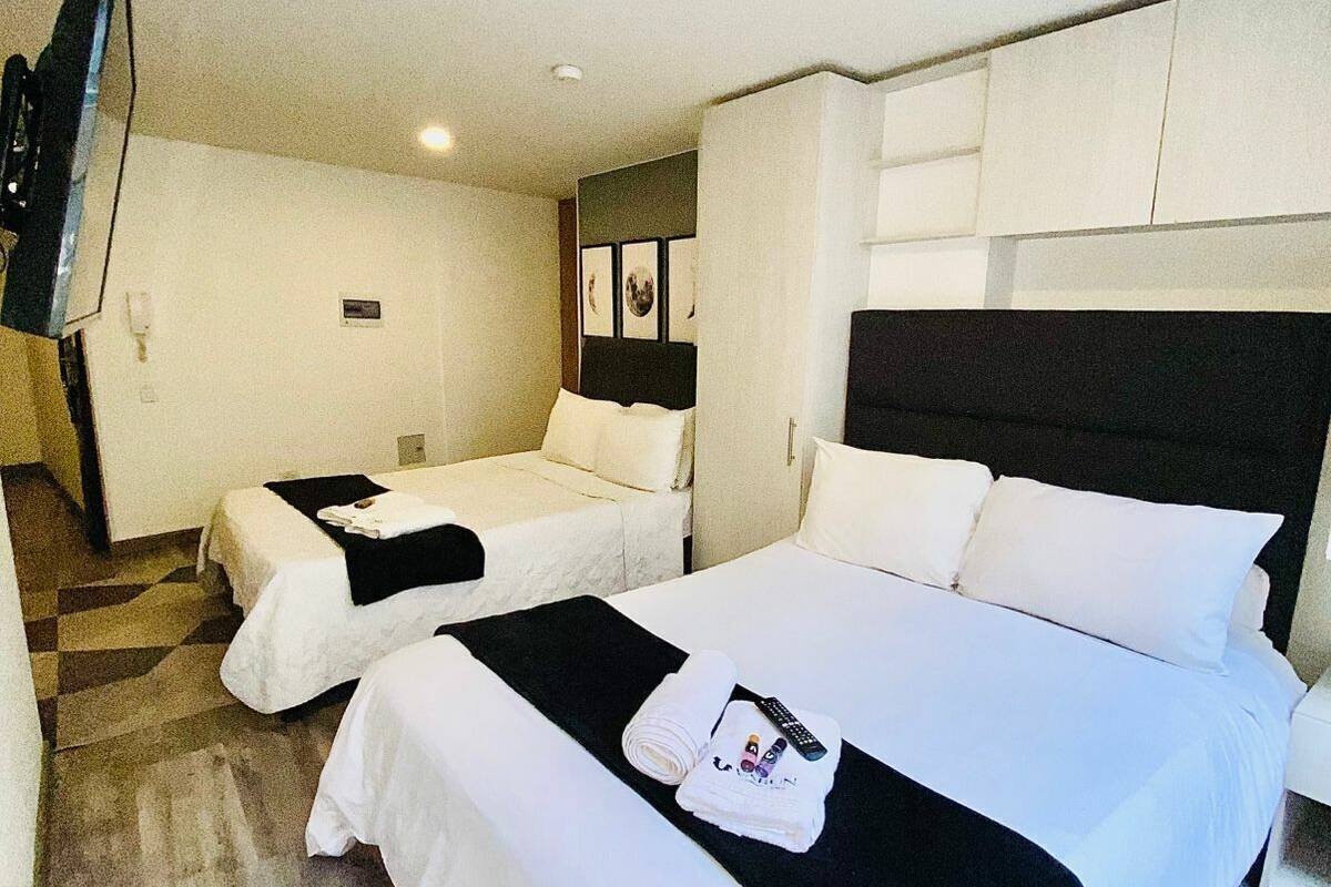 Quarto de hotel com duas camas, uma televisão de tela plana na parede e uma mesinha com artigos de higiene pessoal.
