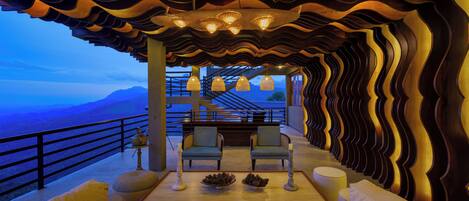Interior moderno com vista panorâmica para as montanhas, com mesa de madeira, assentos acolchoados e escada que dá para uma área externa.