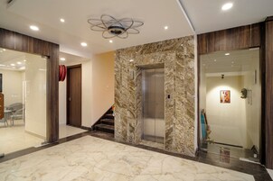 Um hall moderno com piso de mármore, um elevador e uma escadaria.