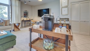 Quarto de hotel moderno com sofá, cafeteira, mesinha de bandeja e uma janela grande.