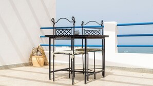 Mesa de metal com duas cadeiras numa varanda, com parede branca e guarda-corpo azul.