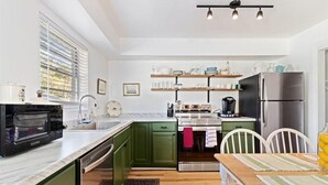 Uma cozinha moderna com armários verdes, uma geladeira de aço inoxidável e uma mesa de jantar de madeira.