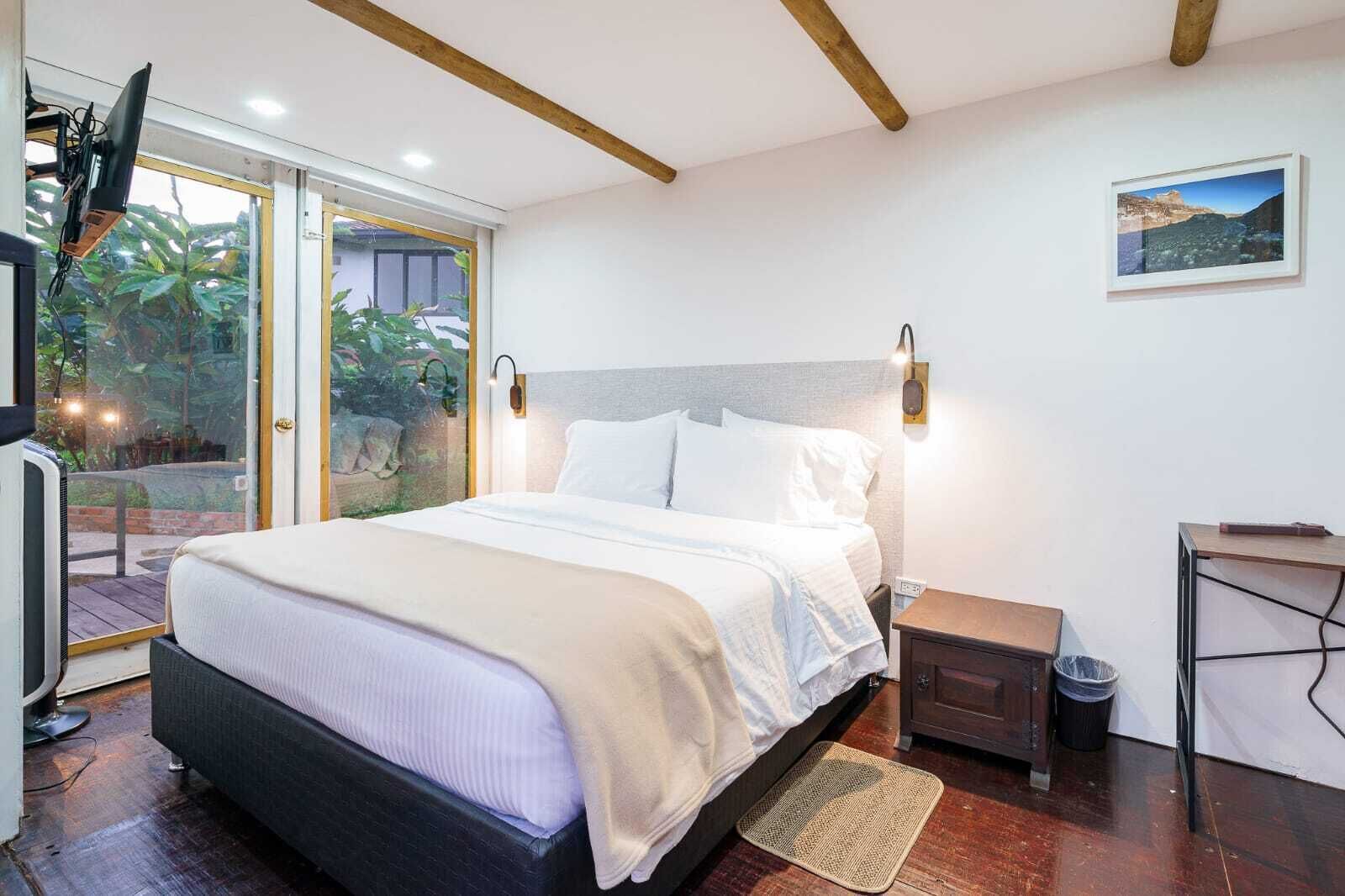 Quarto moderno com uma cama grande, uma escrivaninha e vista para o verde através de uma porta de correr.