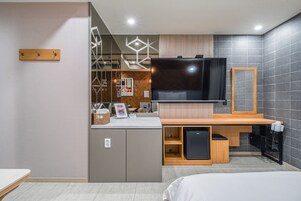 Quarto de hotel moderno com televisão de tela plana grande, móveis de madeira e parede revestida de azulejos.
