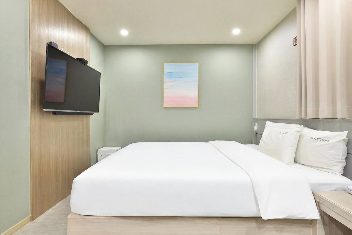 Quarto de hotel com cama, televisão na parede, mesa de cabeceira e um quadro.