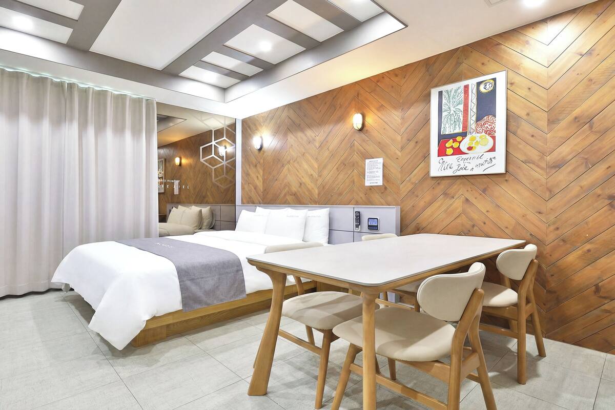 Quarto de hotel com cama, mesa e cadeiras, parede de madeira em padrão herringbone e um quadro na parede.