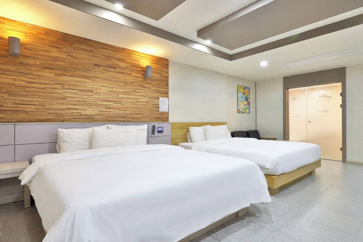 Quarto de hotel com duas camas, parede de destaque em madeira, uma escrivaninha e uma porta.