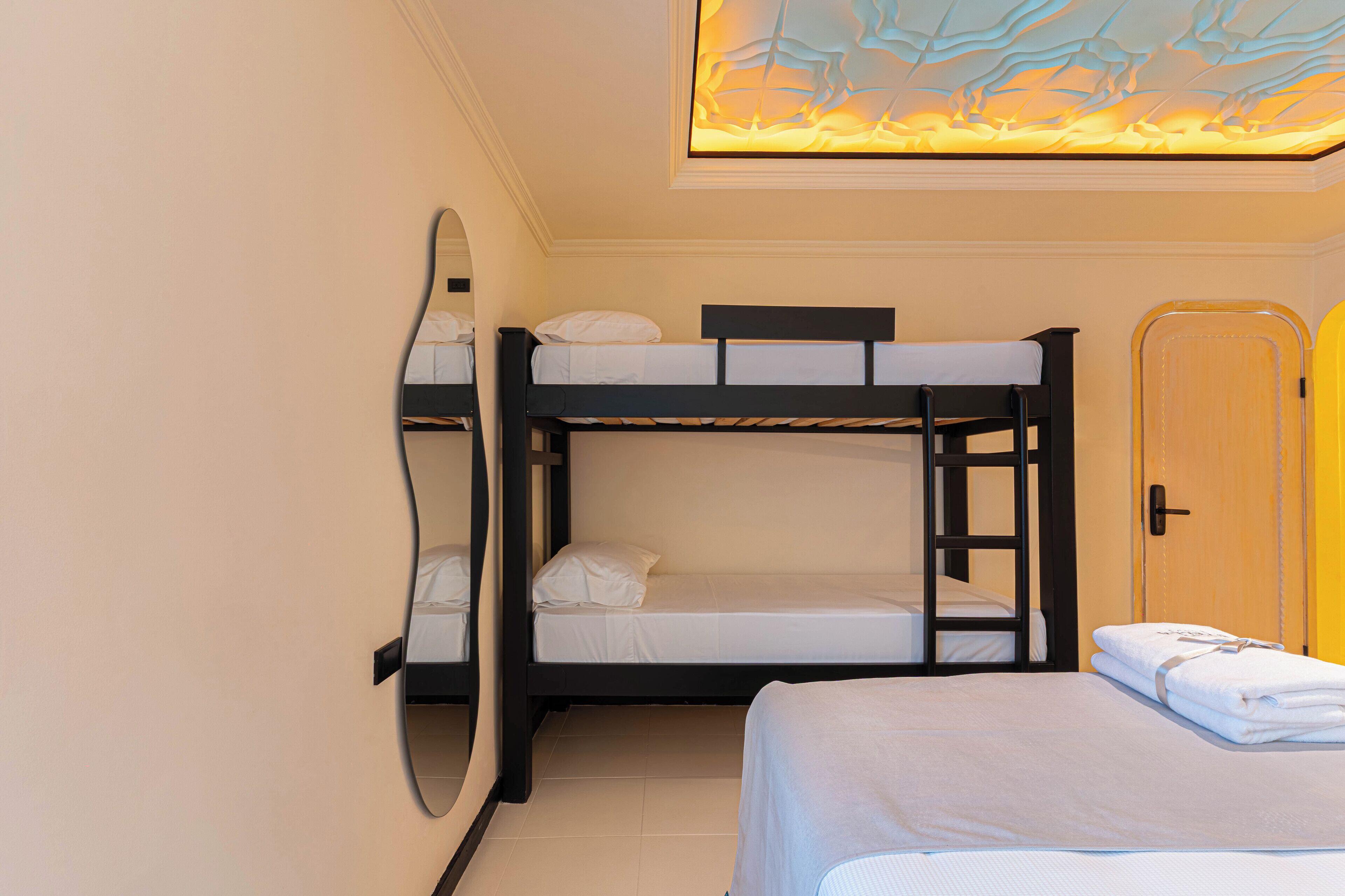 Quarto com beliche, espelho, porta e uma cama com toalha.