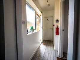 Um corredor estreito com uma janela, uma porta e um extintor fixado na parede.
