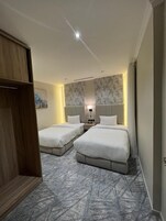 Quarto de hotel com duas camas, um guarda-roupa, um quadro na parede e um carpete estampado.