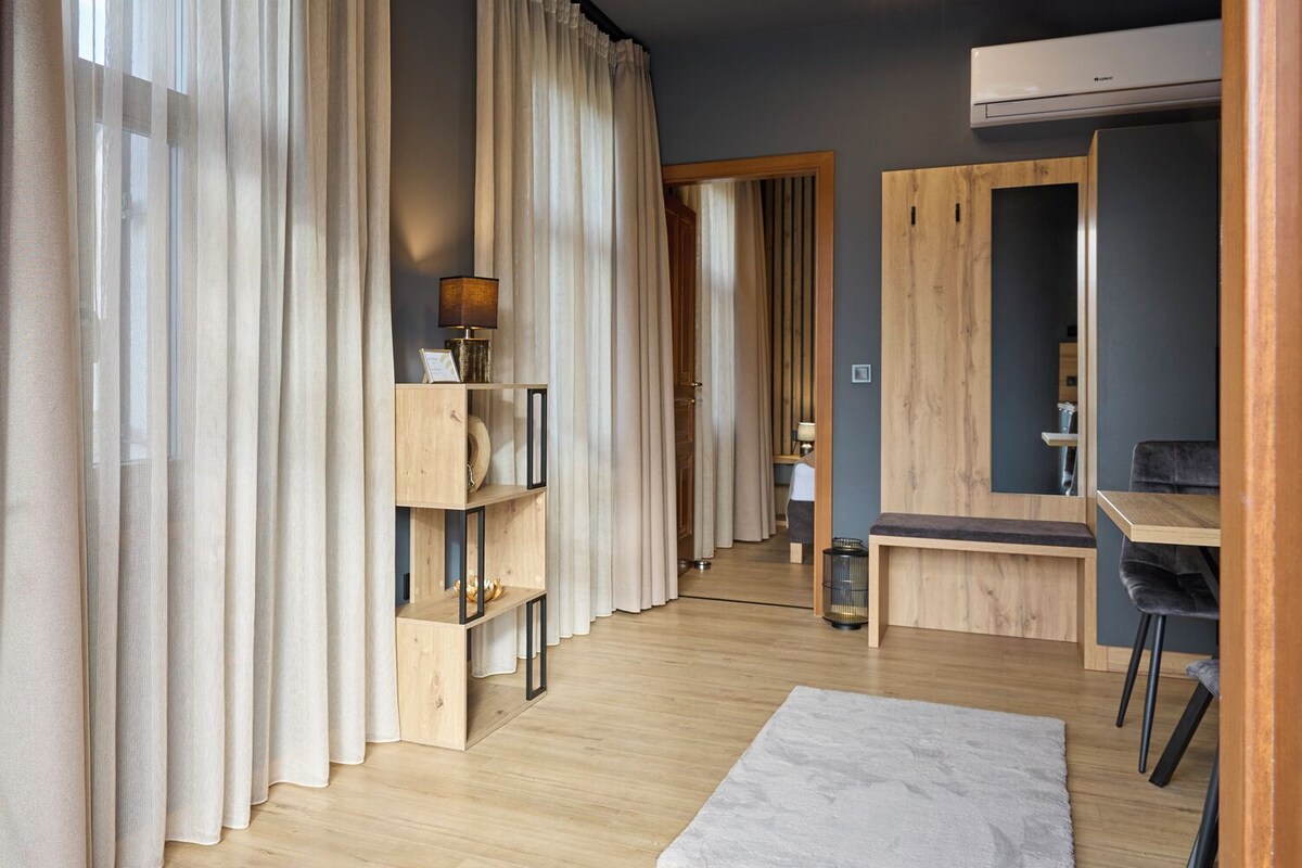 Quarto de hotel moderno com piso de madeira, uma escrivaninha, uma cadeira, um espelho e uma estante de livros.