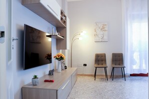 Uma sala de estar moderna com uma TV de tela plana, uma mesinha de console com objetos decorativos, duas poltronas, um abajur e obras de arte na parede.