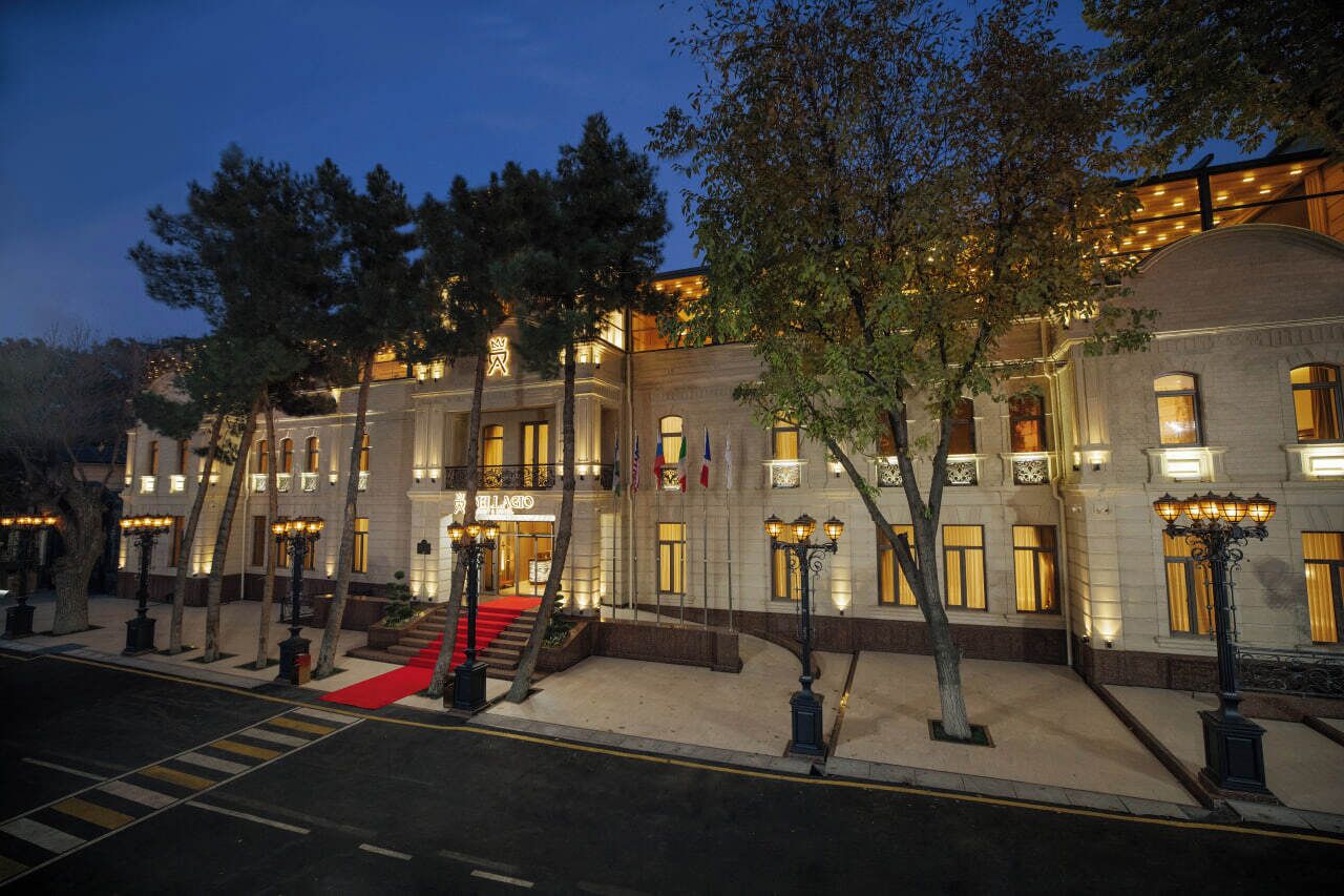 Um hotel imponente com entrada coberta por um tapete vermelho, diversas bandeiras e arquitetura clássica.