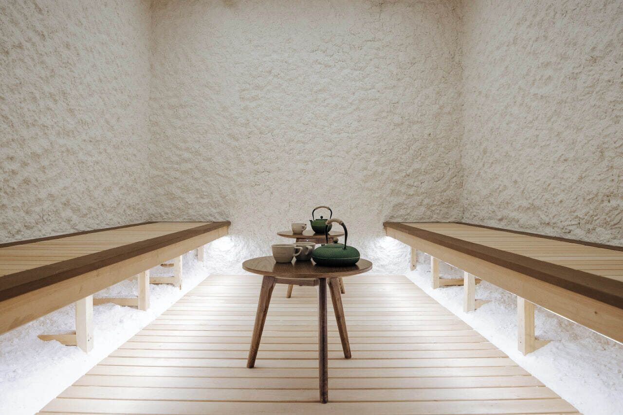 Uma sala de sauna com bancos de madeira e uma mesa central com chaleira e xícaras.
