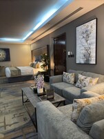 Quarto de hotel moderno com cama, sofá, mesa de centro e obras de arte.