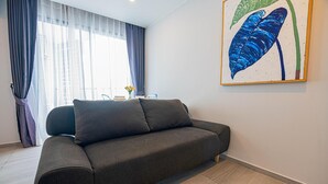 Uma sala de estar moderna com um sofá cinza escuro, uma janela ampla com cortinas leves e um quadro com tema botânico na parede.