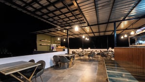 Espaço de refeições ao ar livre com bar, mesas e cadeiras.