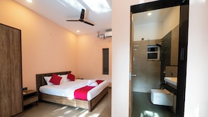 Quarto de hotel moderno com uma cama grande, guarda-roupa, ventoinha no teto e banheiro com pia e espelho.