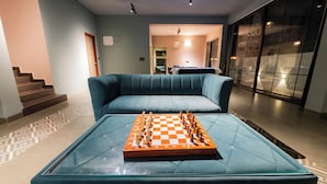 Quarto com um sofá grande e acolchoado, e uma mesa de vidro com um tabuleiro de xadrez.