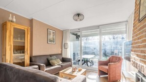 Sala de estar com sofá, mesa de centro e lareira. Porta de vidro dá acesso a uma área externa.