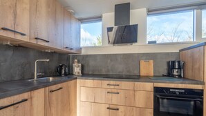 Uma cozinha moderna com armários de madeira, pia de aço inoxidável, forno embutido e uma janela grande que oferece iluminação natural.