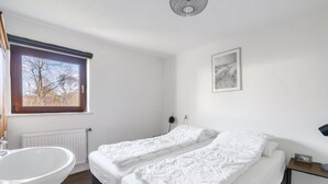 Quarto com duas camas, uma janela grande, pia branca e quadro na parede.