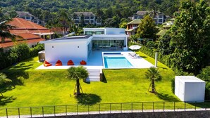 Um hotel moderno com piscina, rodeado por vegetação exuberante e uma paisagem montanhosa.