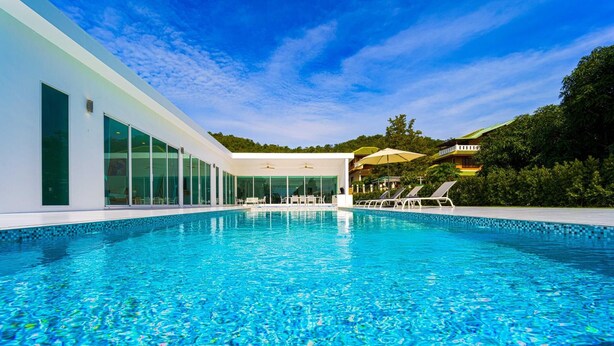 Uma área de piscina moderna com água azul cristalina, cadeiras de sol e um edifício com paredes de vidro.