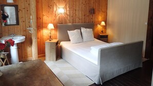 Quarto com cama, abajures, mesa de cabeceira, parede de madeira, espelho e pia.