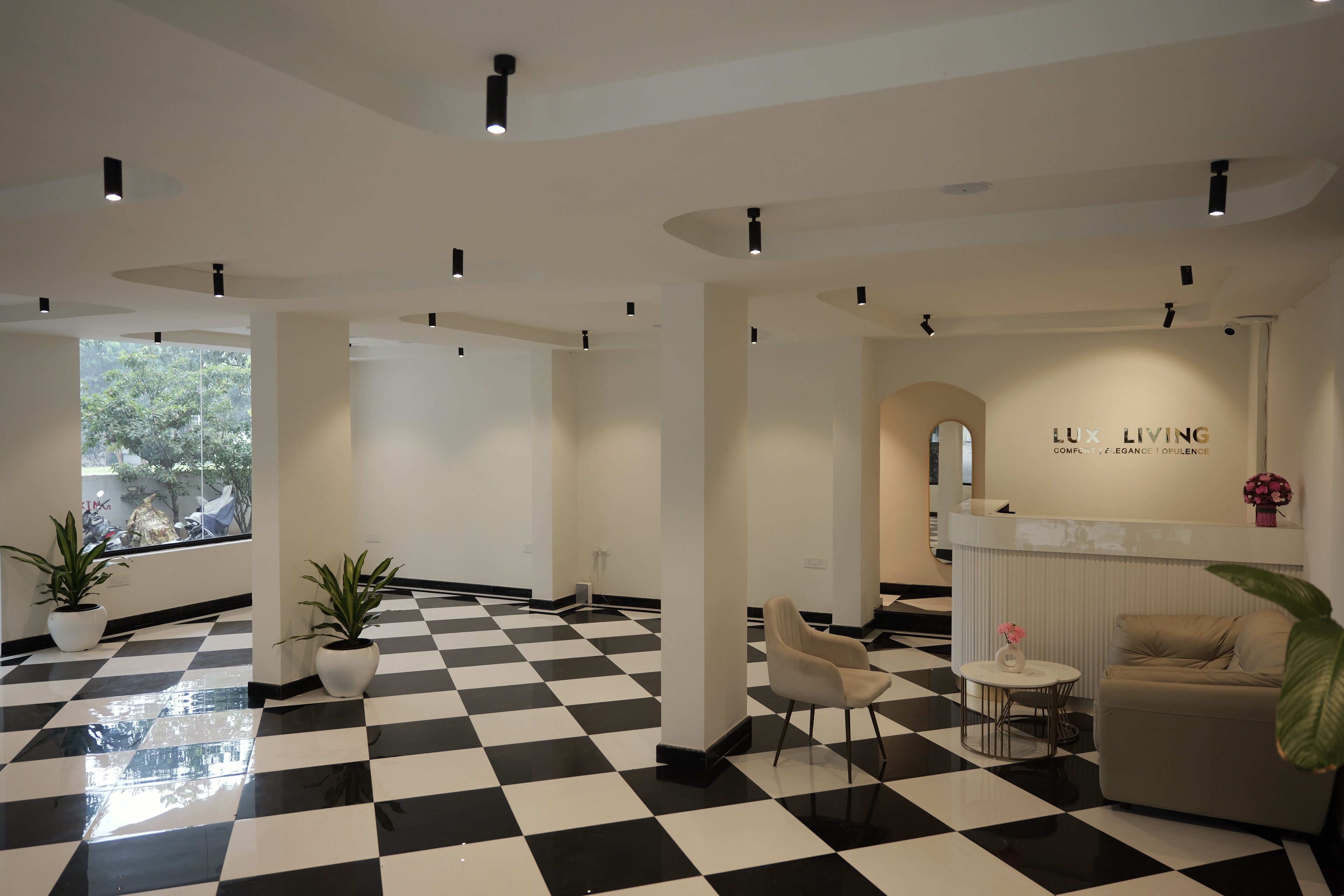 Um saguão de hotel com piso xadrez, plantas em vasos, áreas de estar e um balcão de recepção.