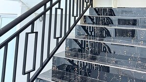 Uma escadaria com guarda-corpos pretos e degraus de mármore.