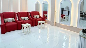 Uma área de estar moderna com sofás vermelhos e pequenas mesas, um espelho grande e um chão de azulejos limpo.