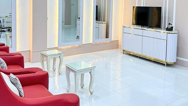 Um quarto espaçoso com piso de azulejos brancos, sofás vermelhos, uma mesa de centro de vidro e um rack branco com uma TV de tela plana.