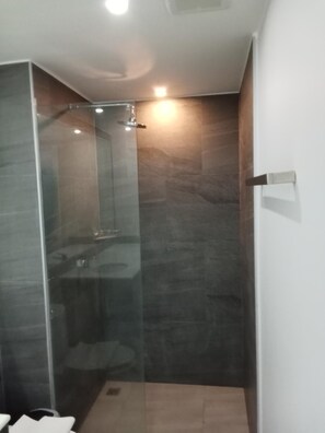 Um banheiro moderno com chuveiro de vidro, espelho e piso ladrilhado.