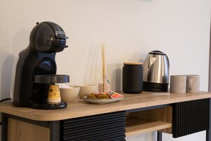 Uma bancada de cozinha com uma cafeteira, uma chaleira, um prato de comida e algumas canecas.