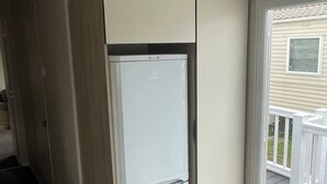 Uma geladeira compacta em uma cozinha compacta, com porta de madeira e acabamento branco.