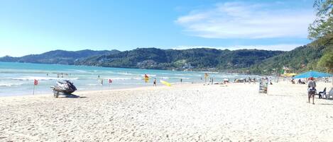 Uma praia arenosa com um jet ski, guarda-sóis e uma bandeira de salva-vidas.