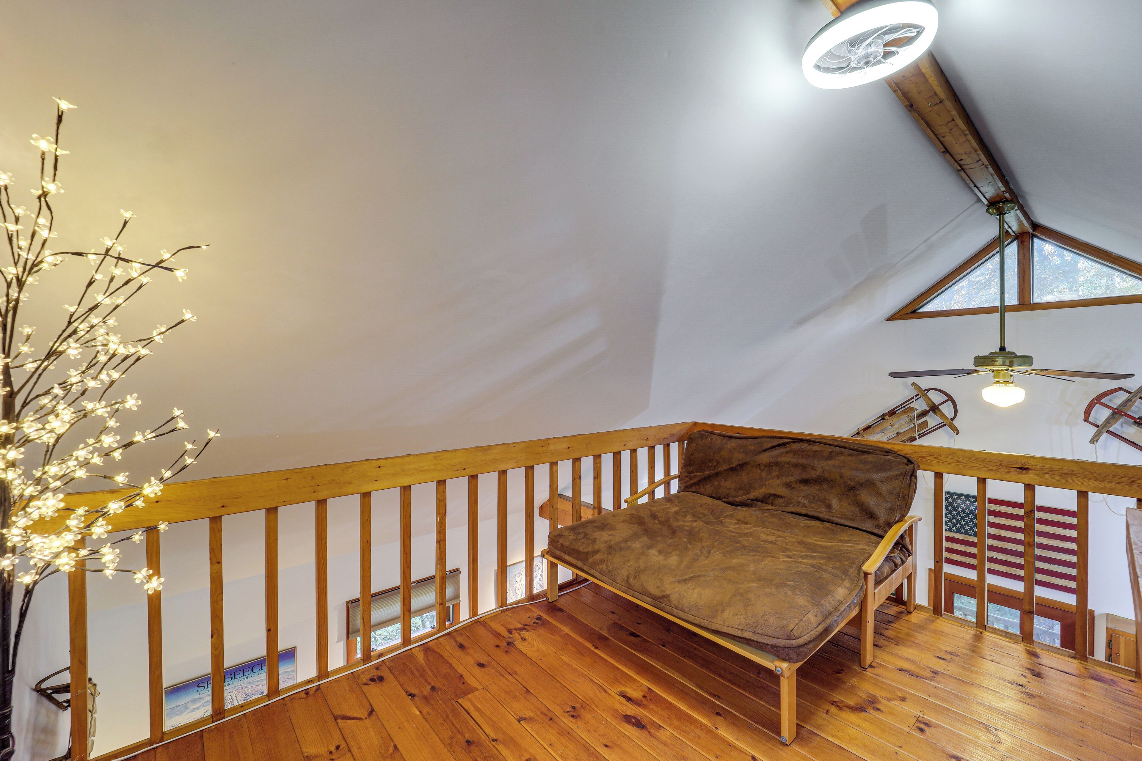 Quarto em estilo loft com piso de madeira, um sofá de couro marrom, corrimão de madeira e ventilador de teto.