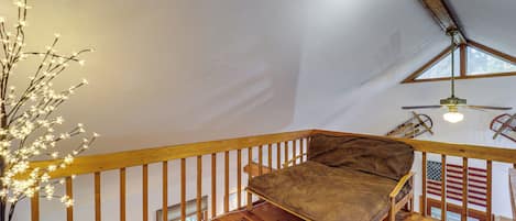 Quarto em estilo loft com piso de madeira, um sofá de couro marrom, corrimão de madeira e ventilador de teto.